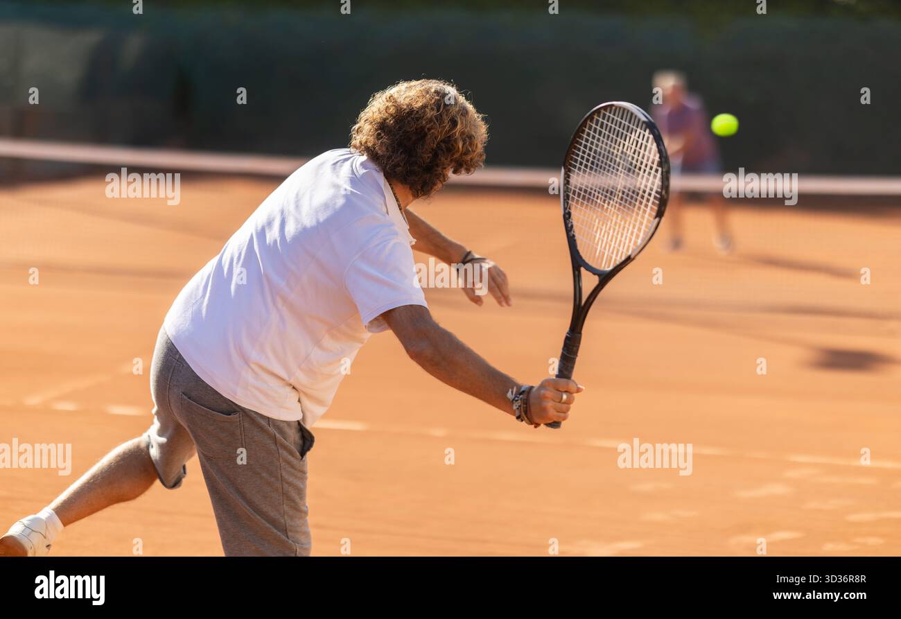 Back view of active male player hitting ball with racket on tennis ...