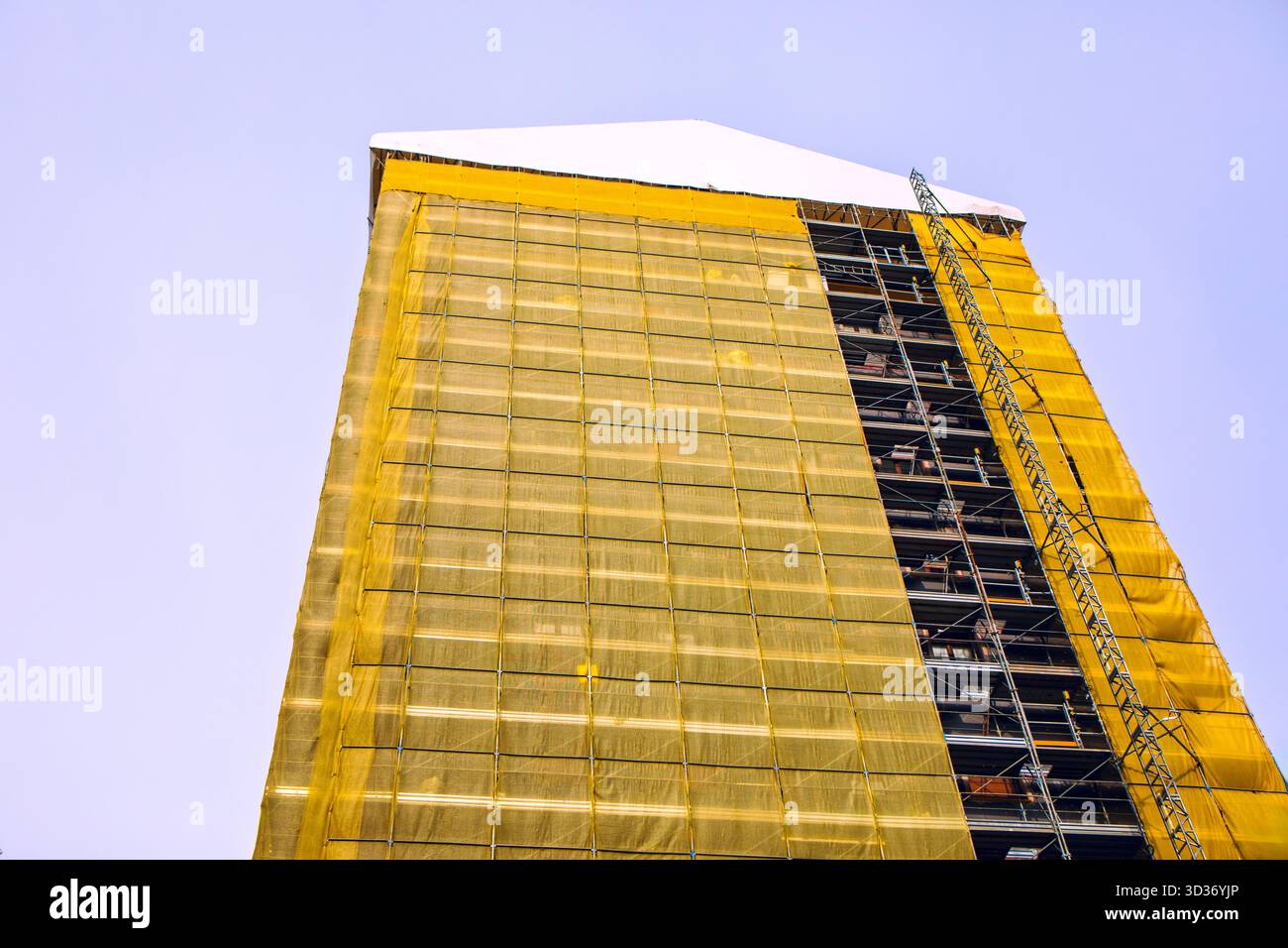 Towering building under construction stands tall, draped in yellow ...