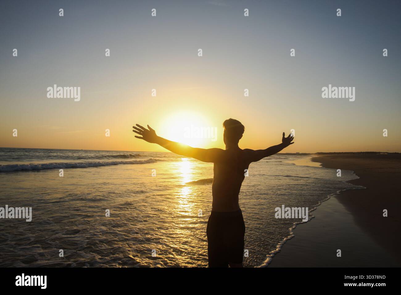 Silhouette of young man, while watching sun going down on the beach ...