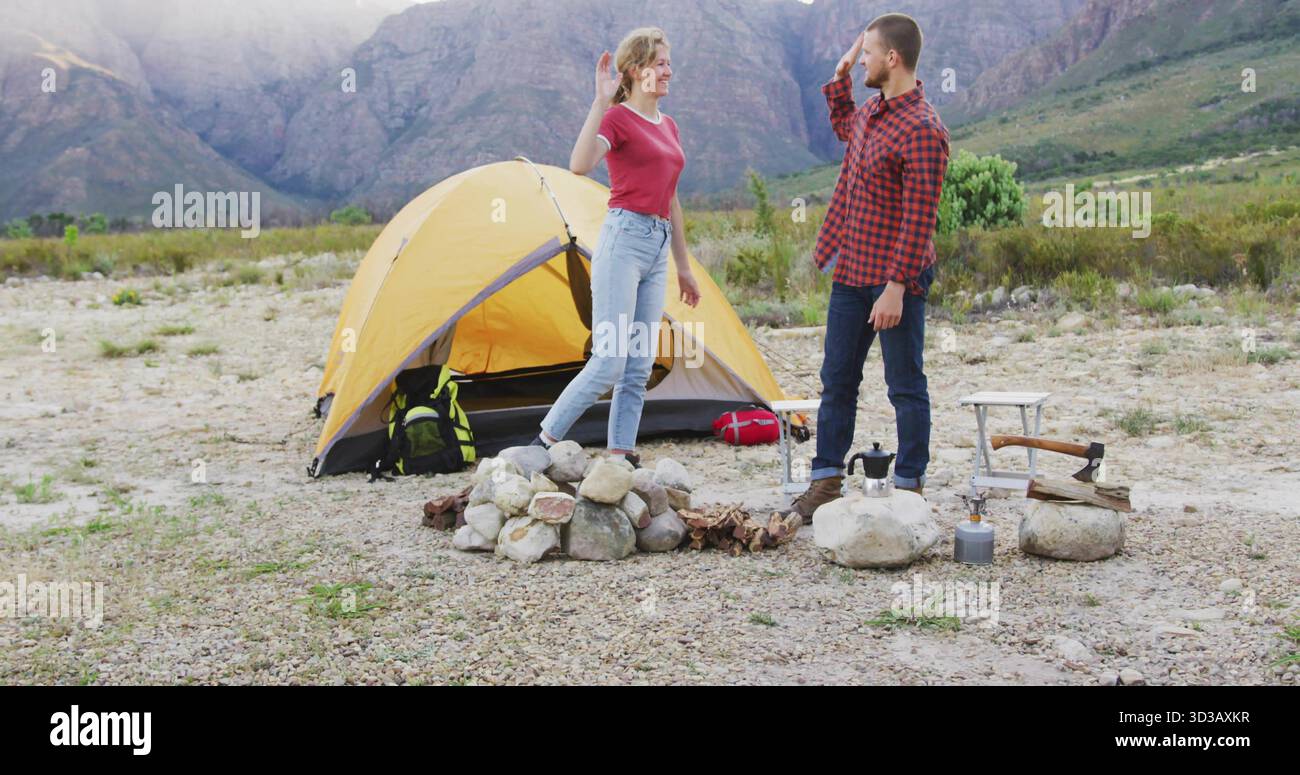 Raising hands man and woman greeting each other at rocky campsite, with ...