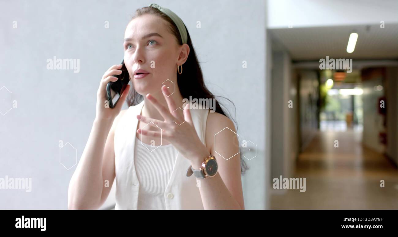 Talking woman wearing smartwatch using smartphone in office corridor ...