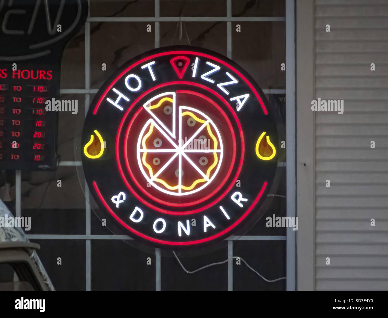 A vibrant neon sign illuminates a storefront, advertising Hot Pizza and ...