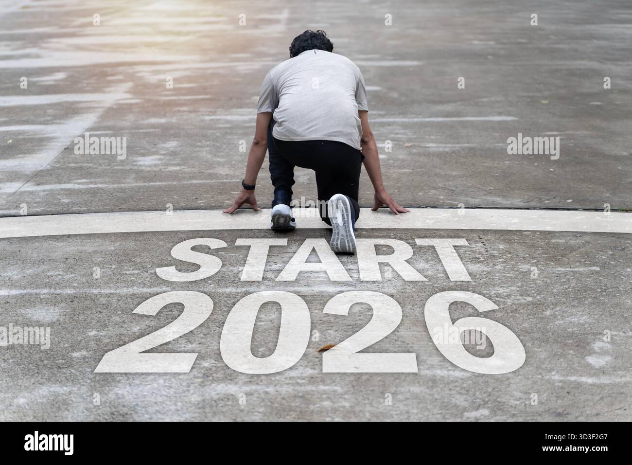 A man kneeling on a start line marked 2026 representing motivation ...