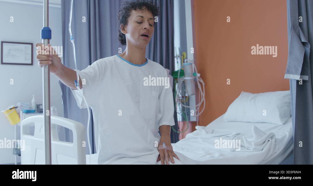 Patient holding IV pole and resting hand on leg in hospital room, with ...