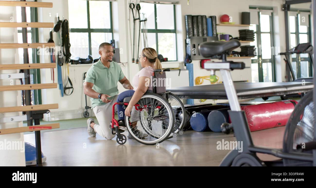 Kneeling therapist in green polo helping manual wheelchair client in ...