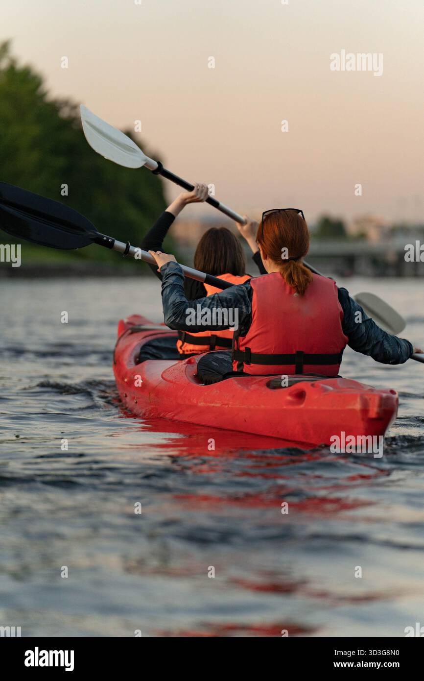 Two women paddling a tandem kayak from behind Stock Photo - Alamy