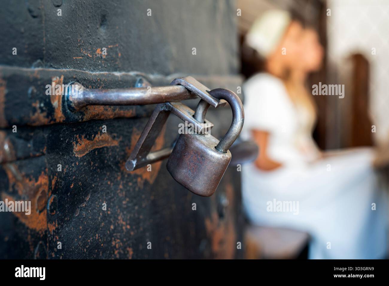 Steel door with padlock, behind it blurred figures of young women ...
