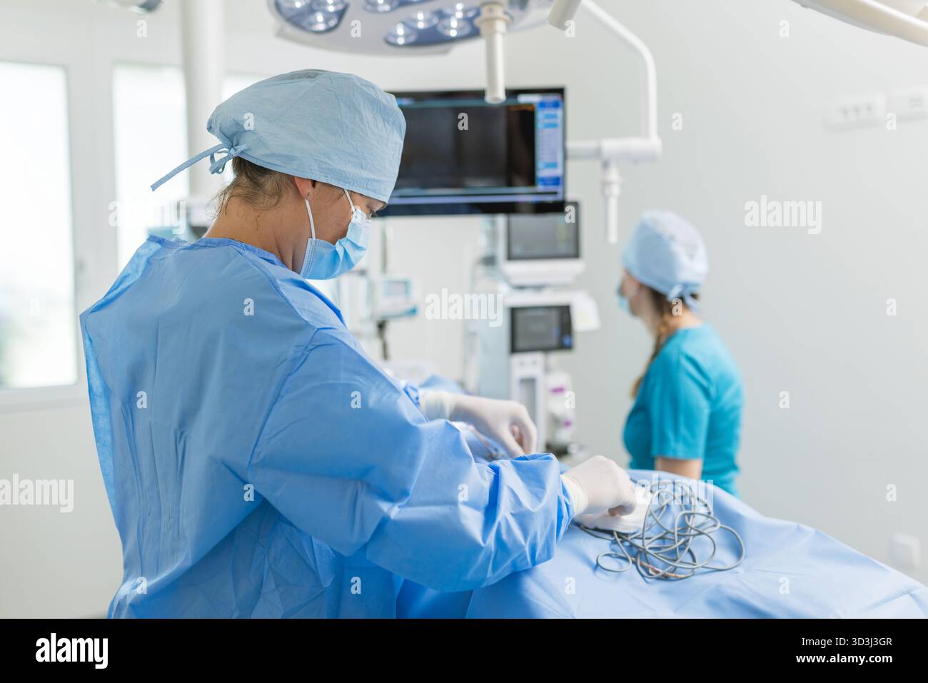 Two medical professionals in sterile attire get ready for a surgical ...