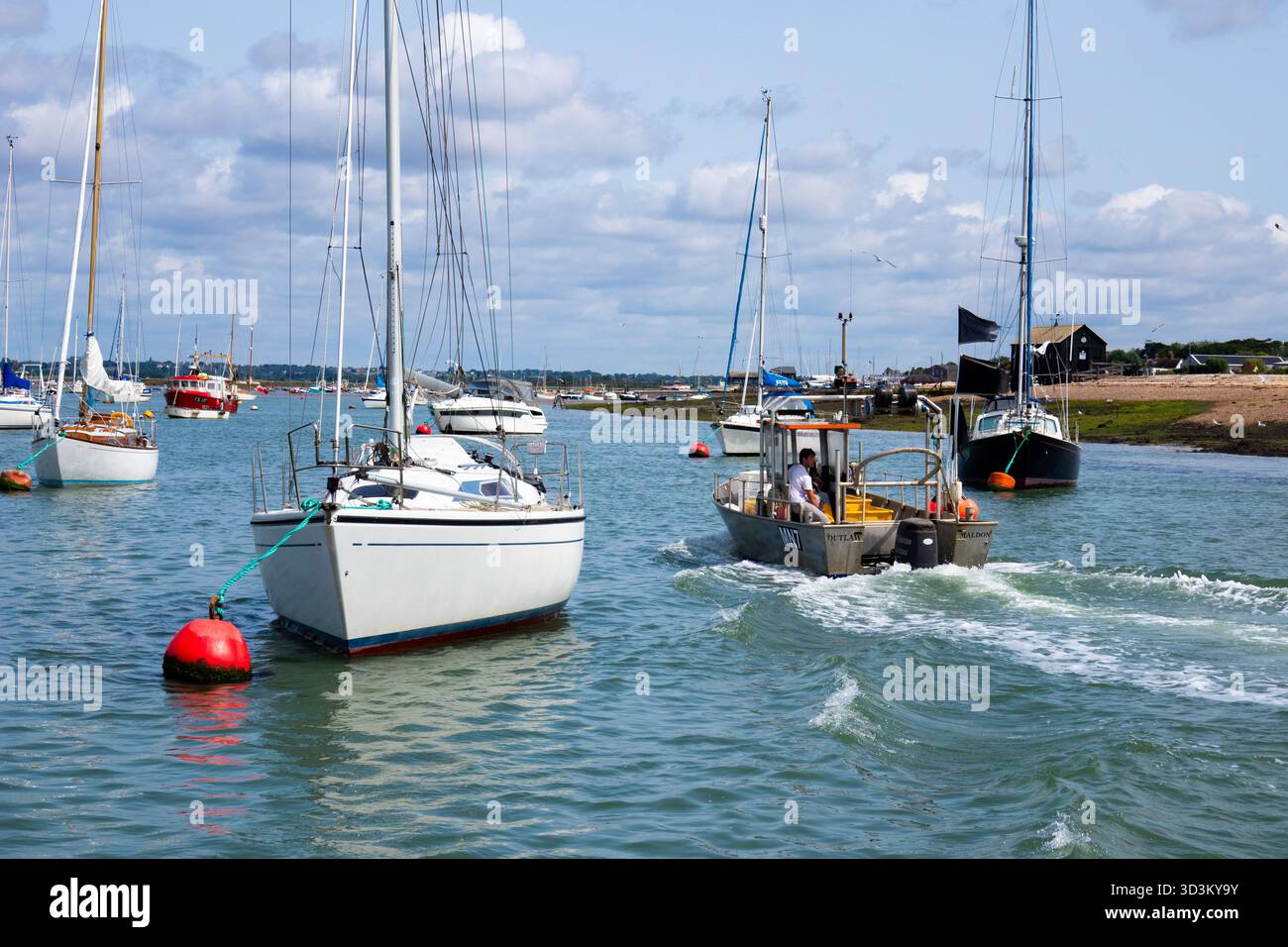 Yachts moored on swinging moorings with boat passing at West Mersea ...