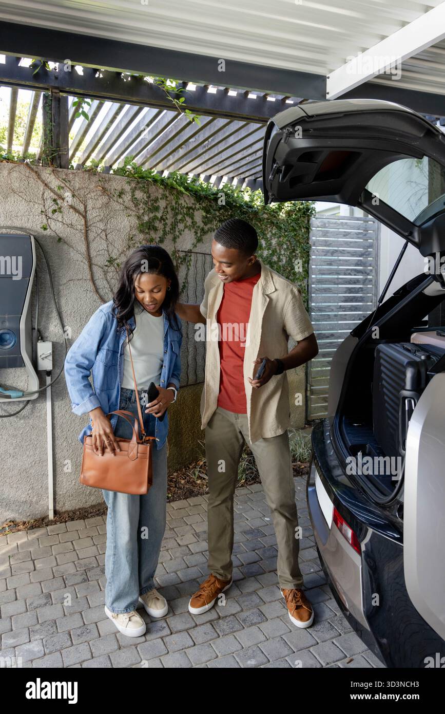 African American couple standing under carport, holding smartphones ...