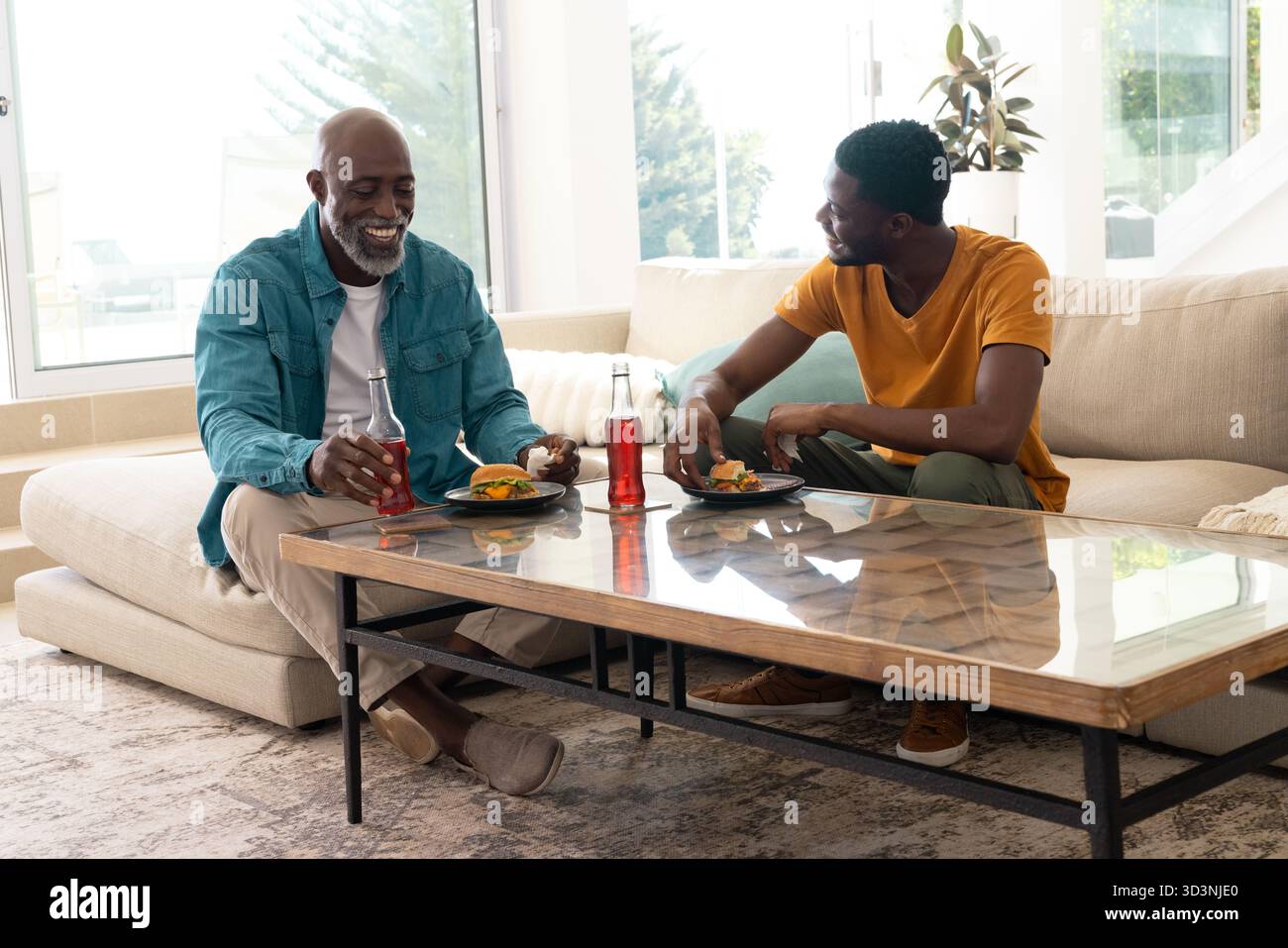 Sharing African American father and son eating burgers on sofa in ...