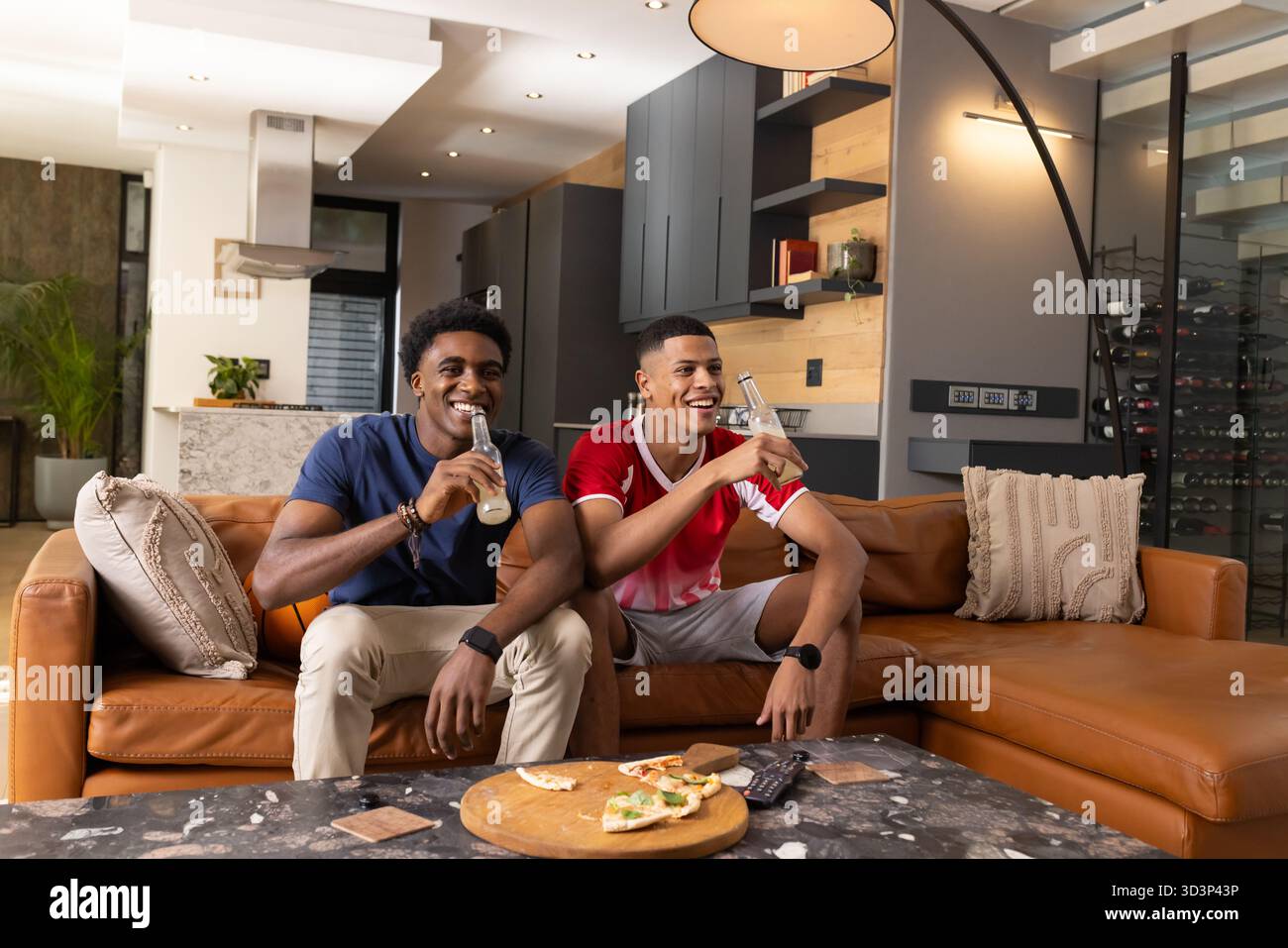 Diverse male friends laughing and drinking from bottles in modern ...