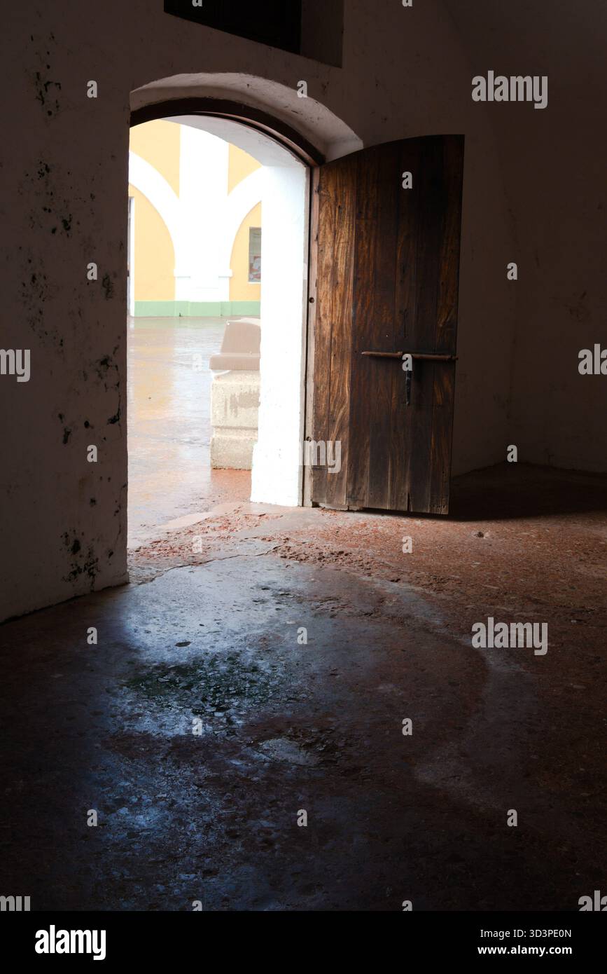 A partially open wooden door allows sunlight to stream into a dimly lit ...