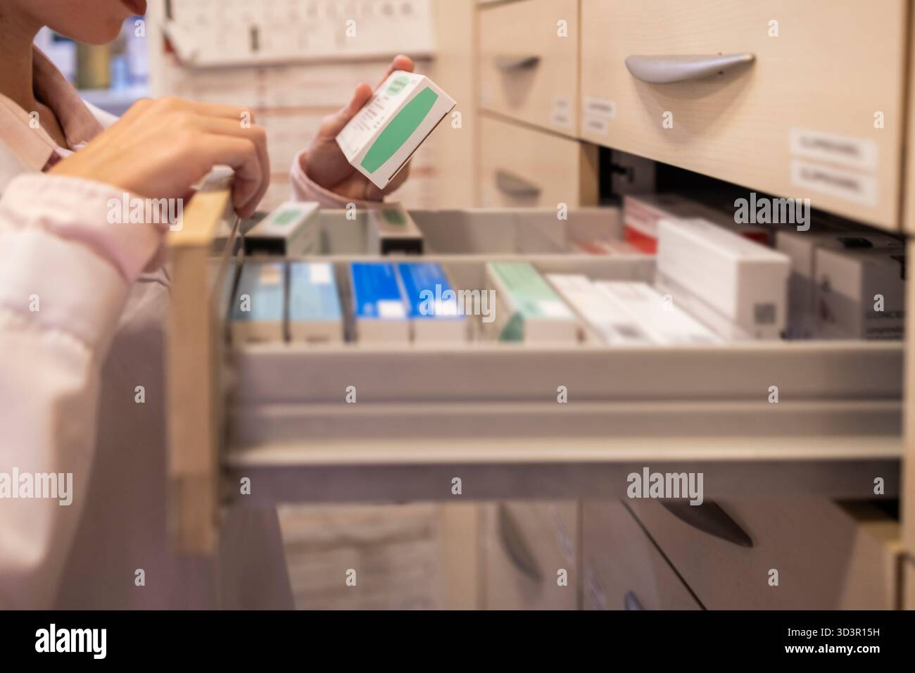 A pharmacist organizes medication boxes in a pharmacy drawer, ensuring ...
