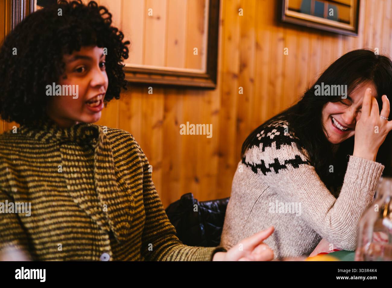 Women of Asian and Hispanic descent laugh together in wood restaurant ...