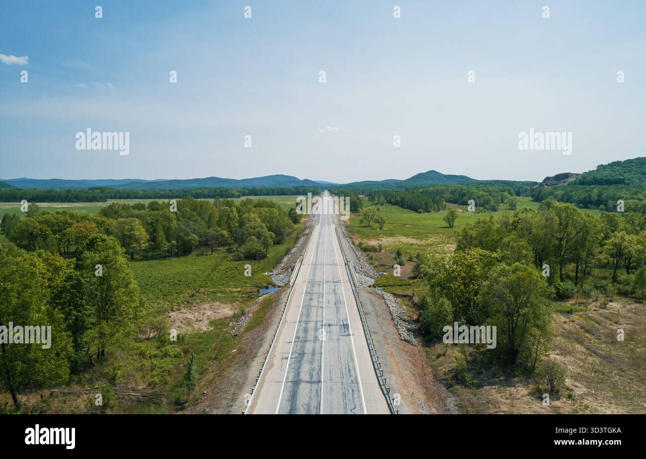 Wide empty road stretches through green landscape in sunny weather near ...
