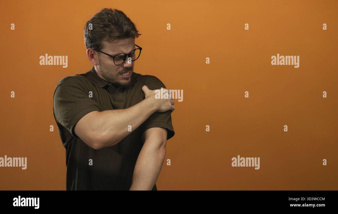 Young hispanic man clutching shoulder with pained face in studio ...
