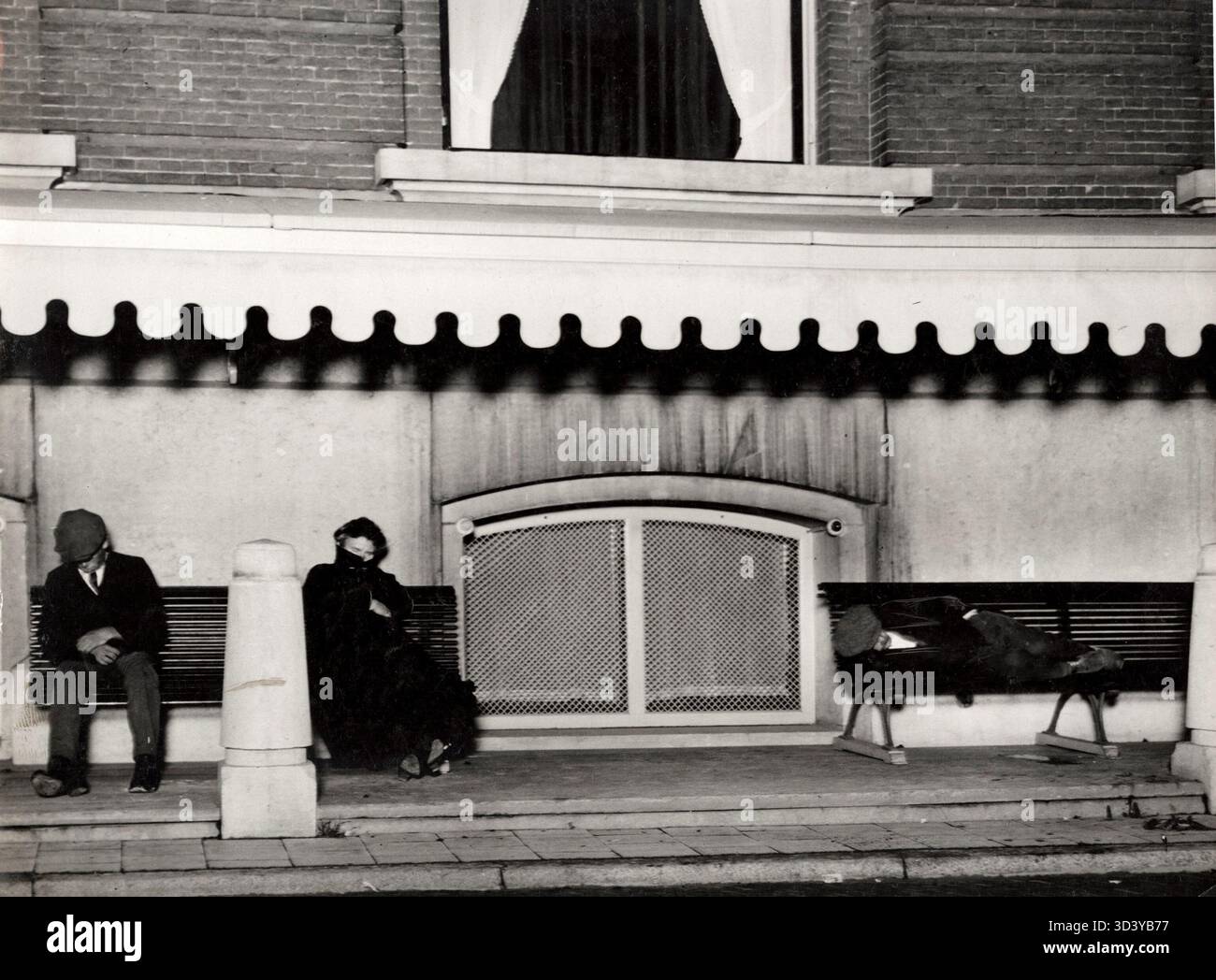 Two vagrants are shown sleeping on a bench under the awning of the ...