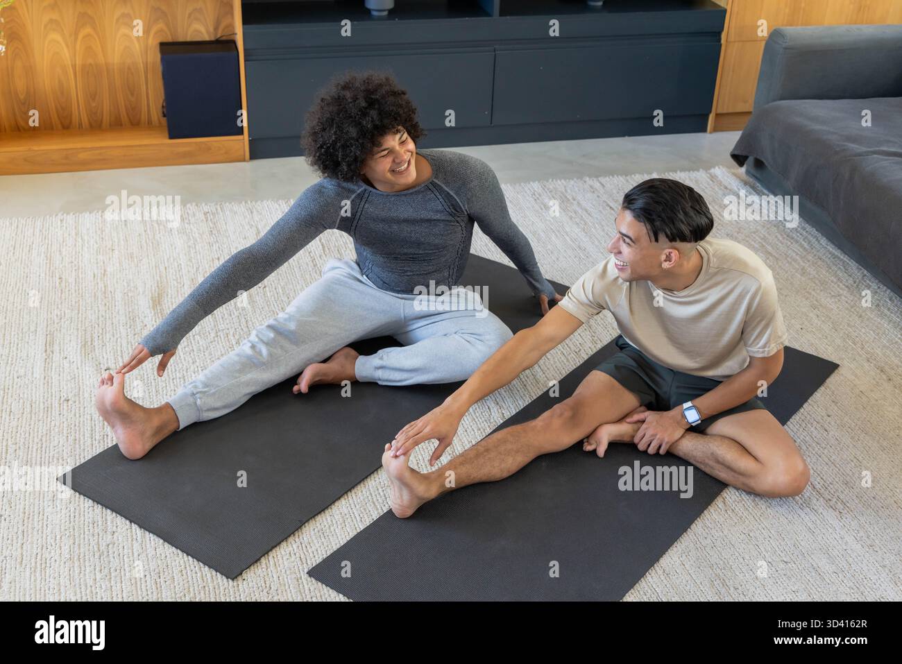 Diverse male friends stretching legs on black yoga mats in modern ...