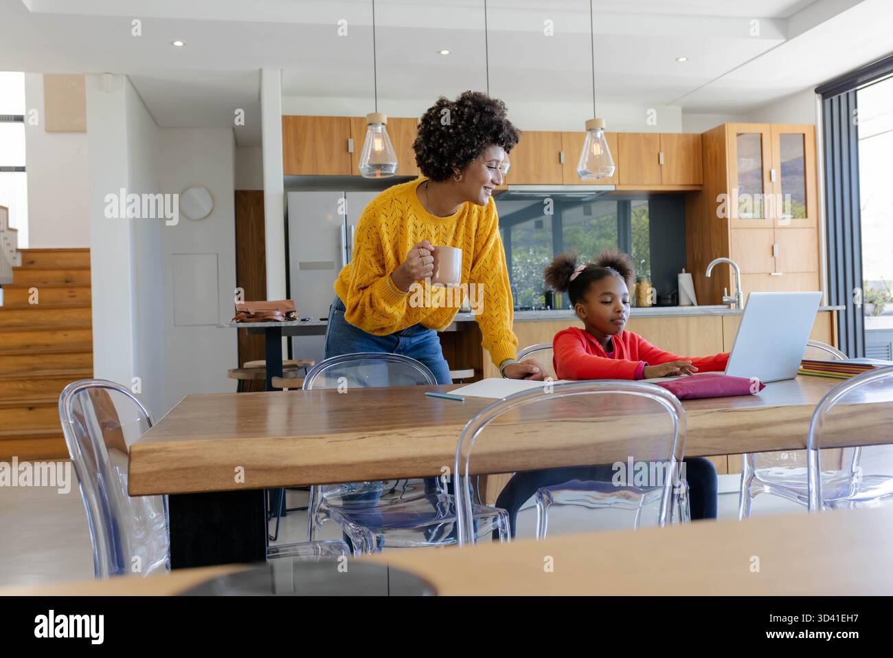 Smiling Diverse mother and daughter leaning over dining table in ...