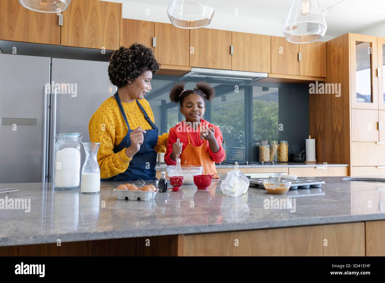 Diverse mother and daughter mixing batter in modern kitchen, with whisk ...