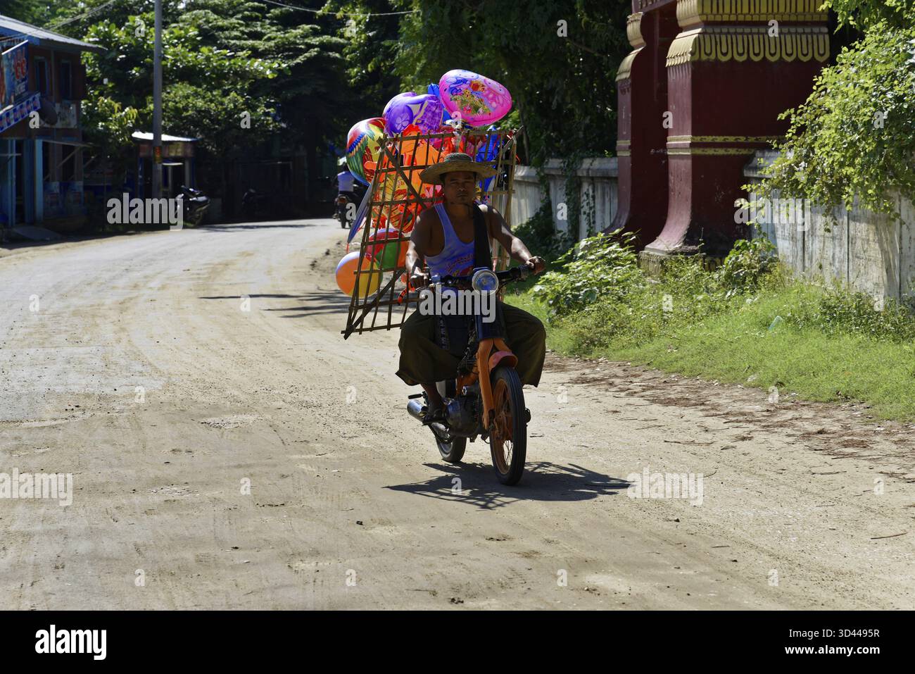 A man transports colorful goods on a motorcycle along a road, Mingun ...