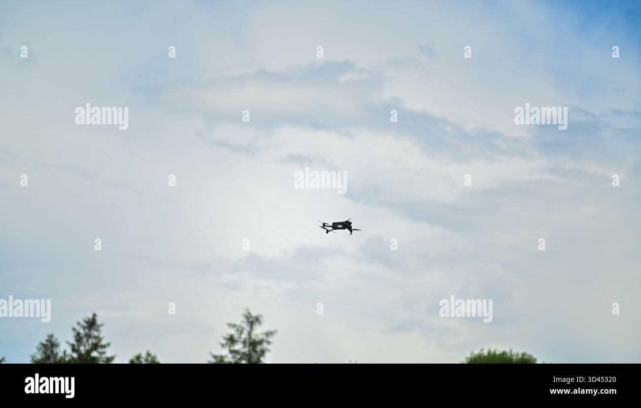 drone is soaring through a clear sky, with a backdrop of white clouds ...