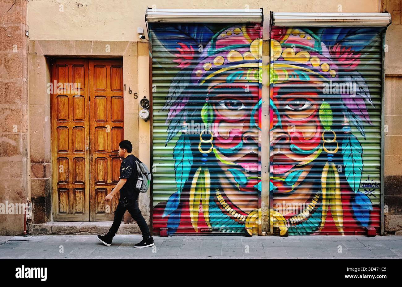 Man walking past a vibrant street mural of an indigenous warrior face ...