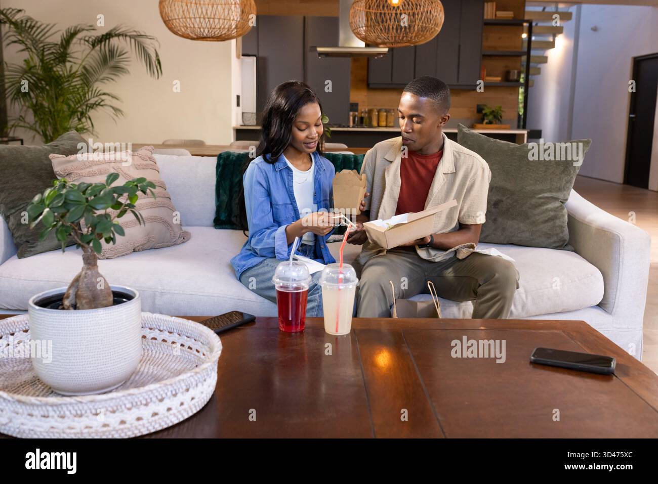 Sharing African American couple eating takeout on sofa in open-plan ...
