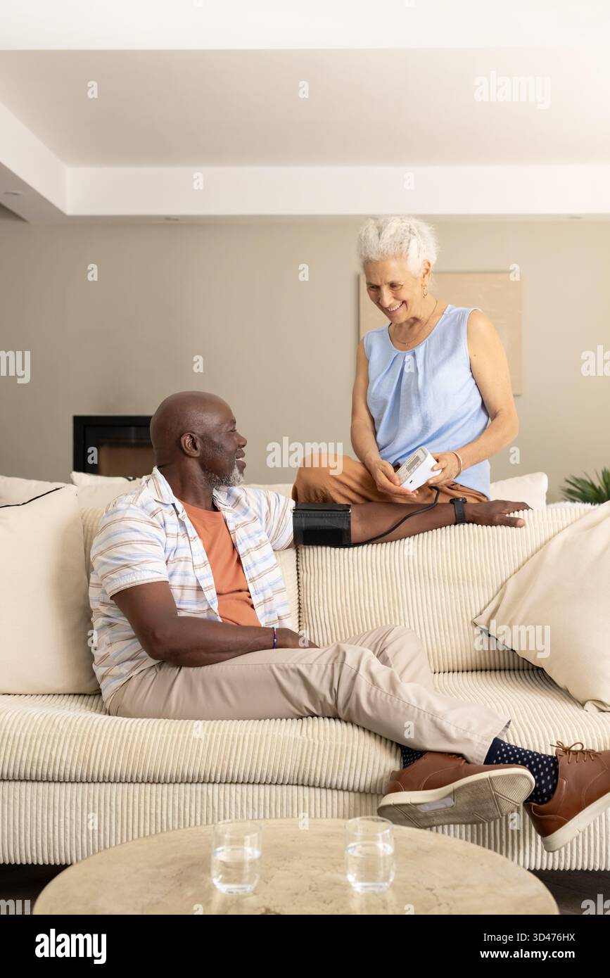 Diverse senior couple checking blood pressure on couch in living room ...
