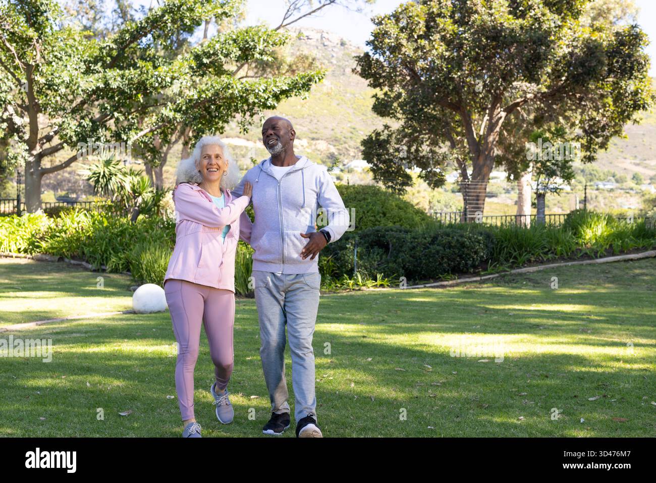 Walking senior couple arm in arm strolling on manicured garden lawn ...
