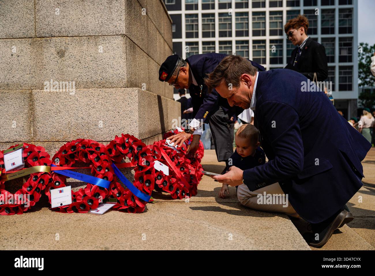 A man and a baby looking at Remembrance flower circles at the Cenotaph ...