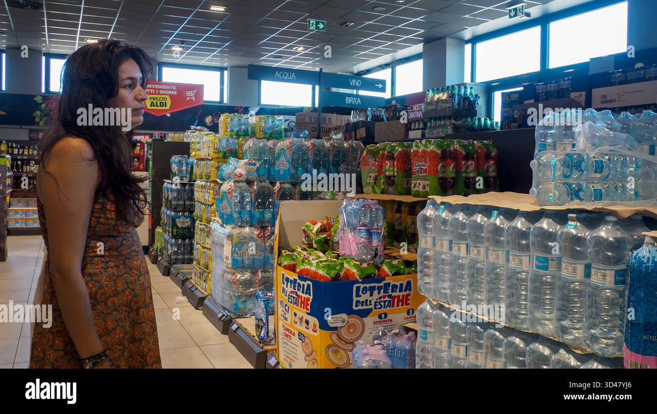 Cremona, Italy August 11th 2025 Shopper comparing bottled water and ...