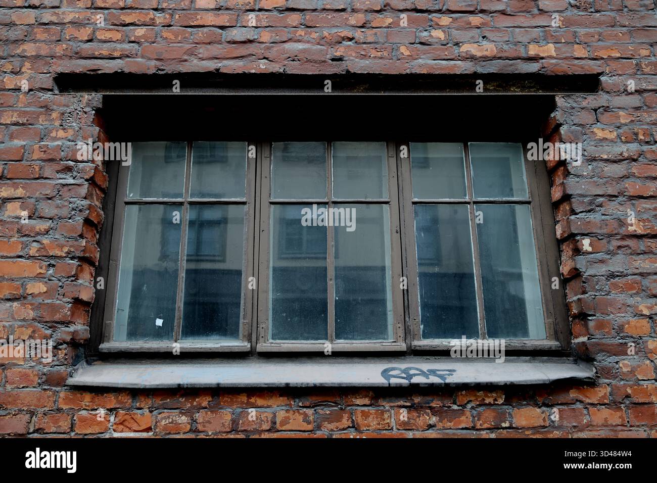 Weathered multi-pane wooden window in a red brick wall with worn mortar ...