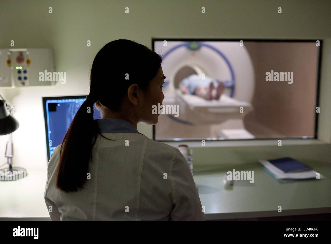 Rear view of female doctor checking image on computer while her patient ...