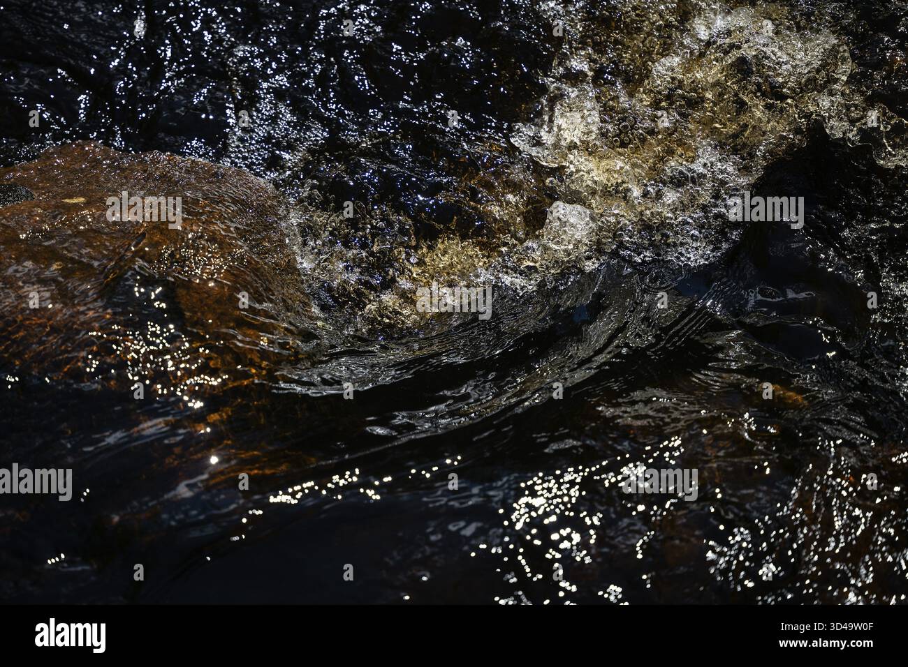 Stream flow with dark water, reflections of light and turbulence ...