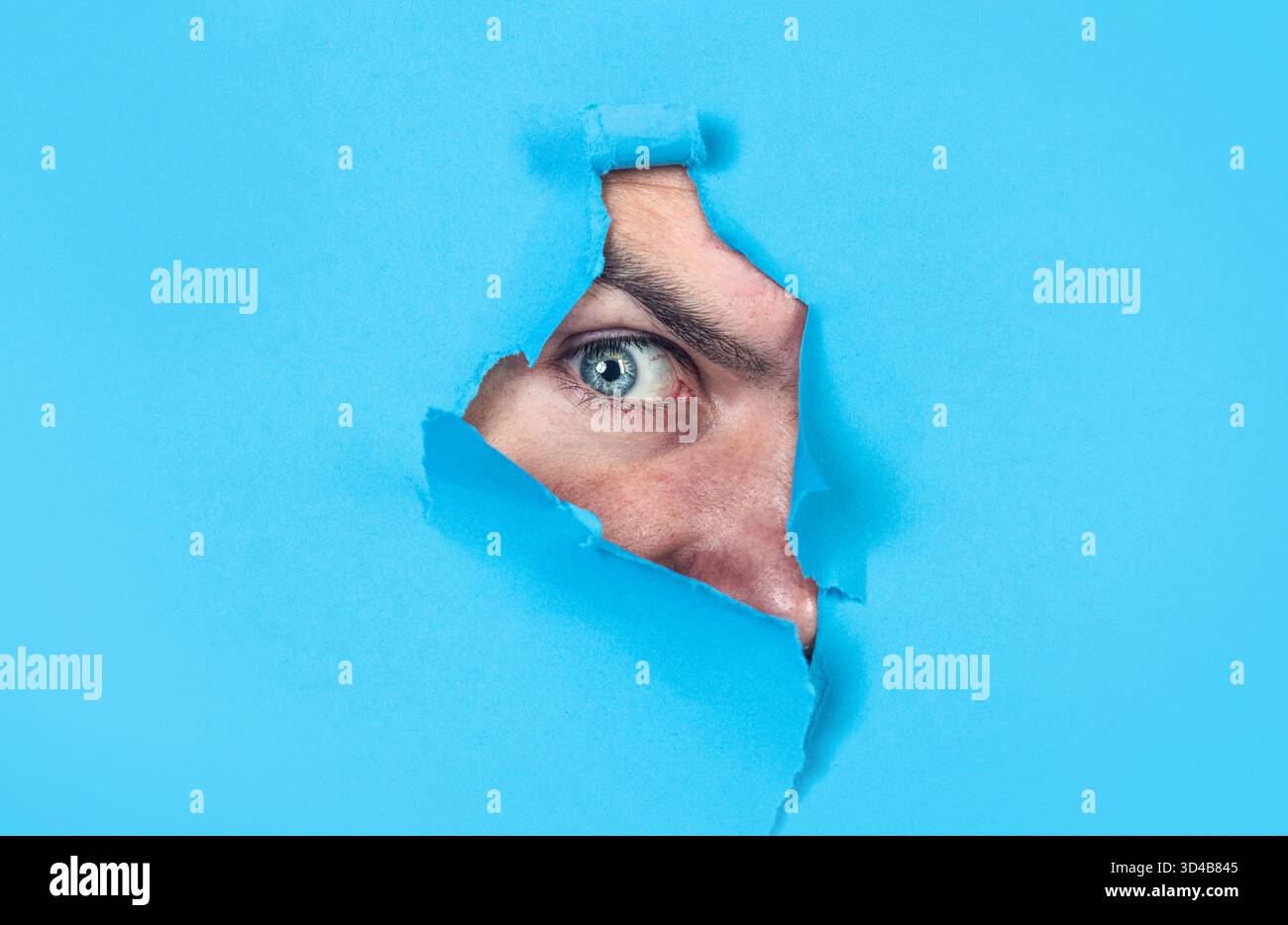 Man's eye looking through hole. Man looking through hole in blue paper ...