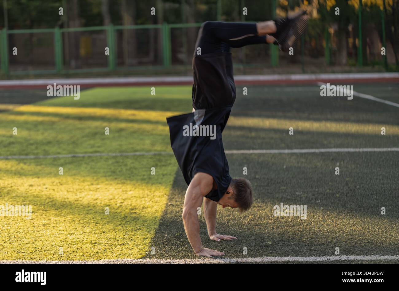 man balances in a handstand on a football field. He wears headphones ...
