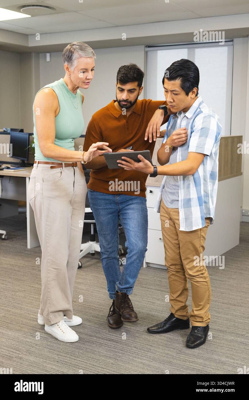 Discussing Diverse coworkers pointing at tablet computer in open plan office, with desktop ...