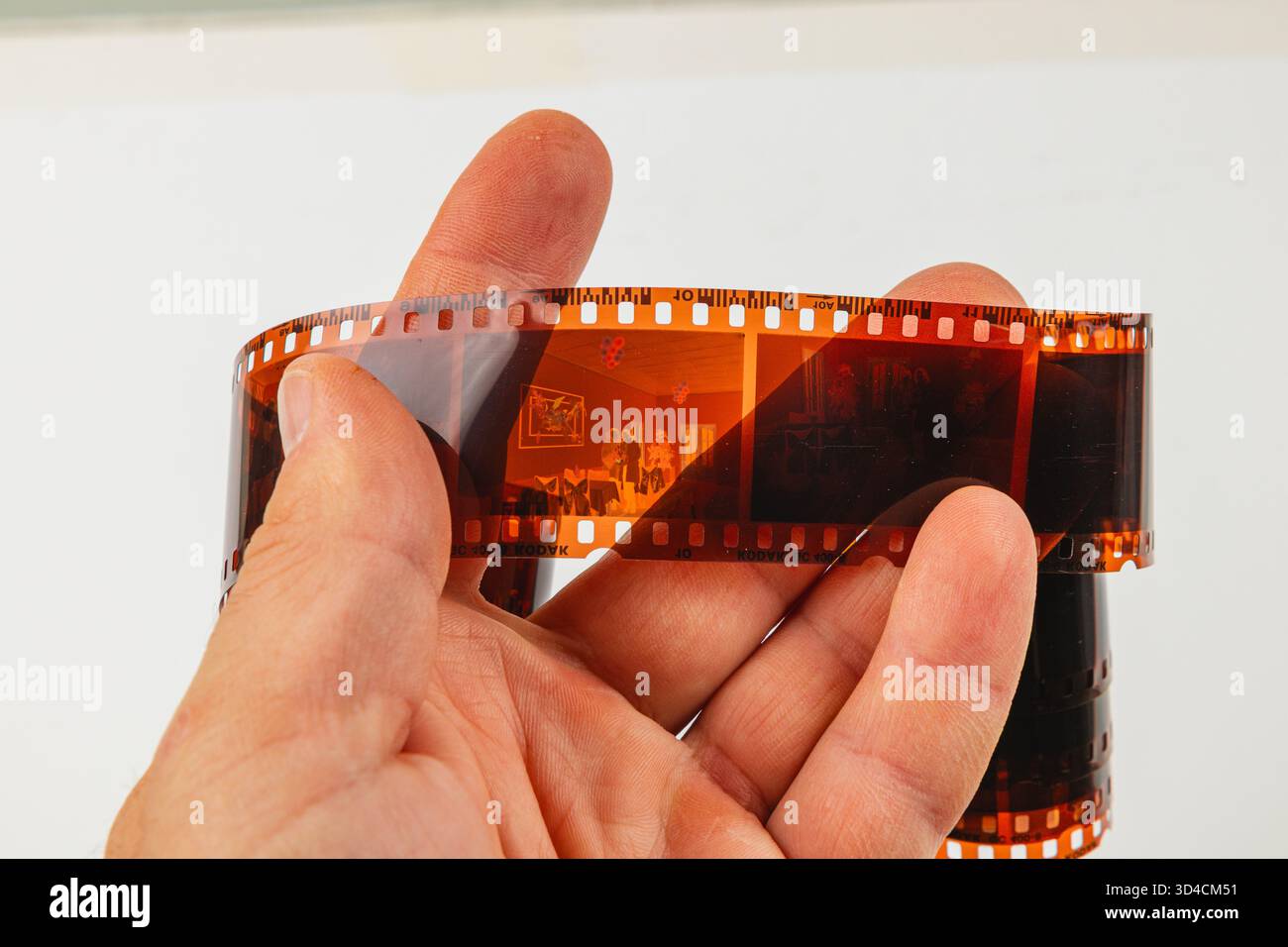 A hand grips an old film strip showing faded images. The scenes are ...