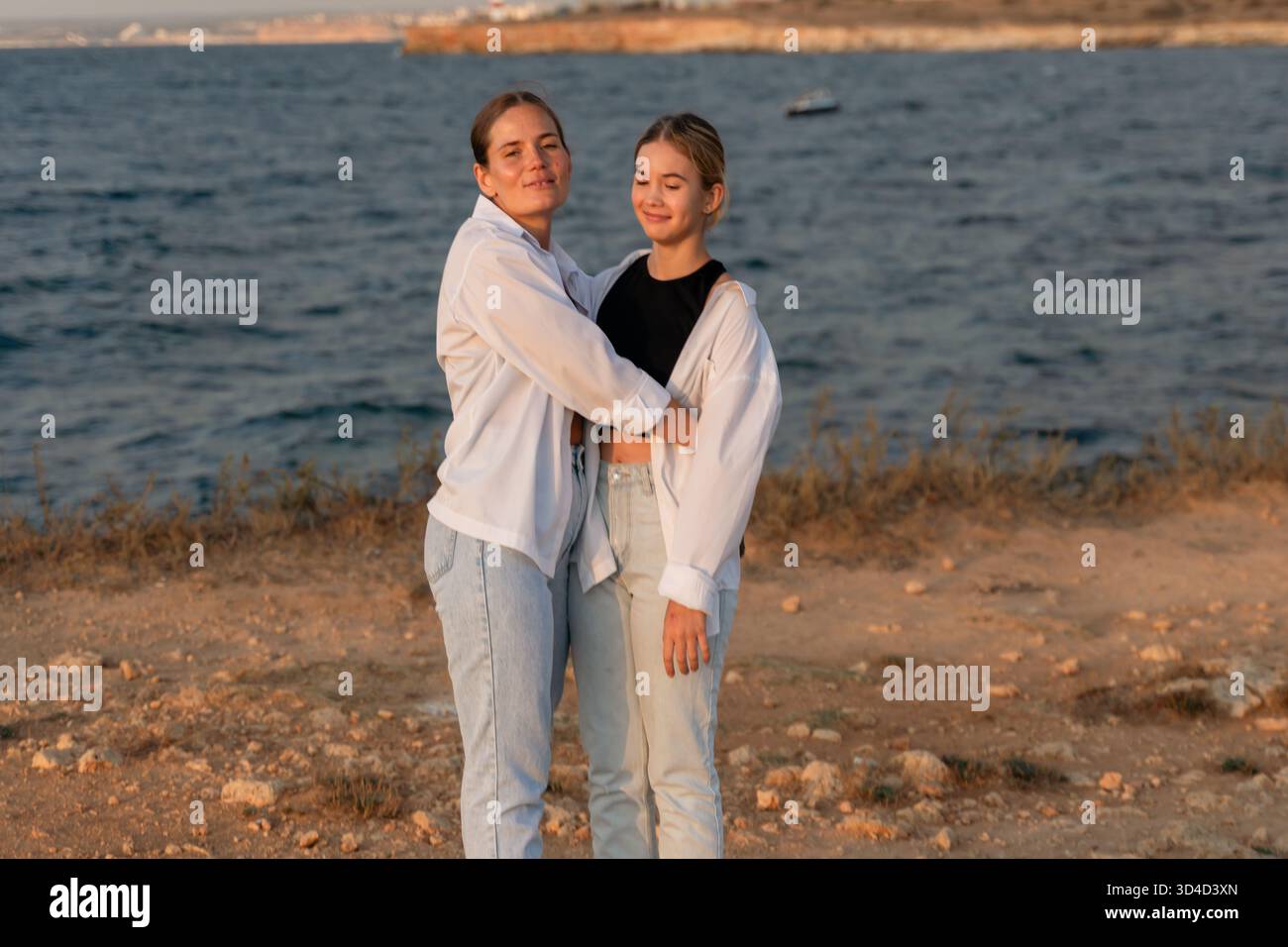 A young couple stands on a beach, the man with his arm around the woman ...