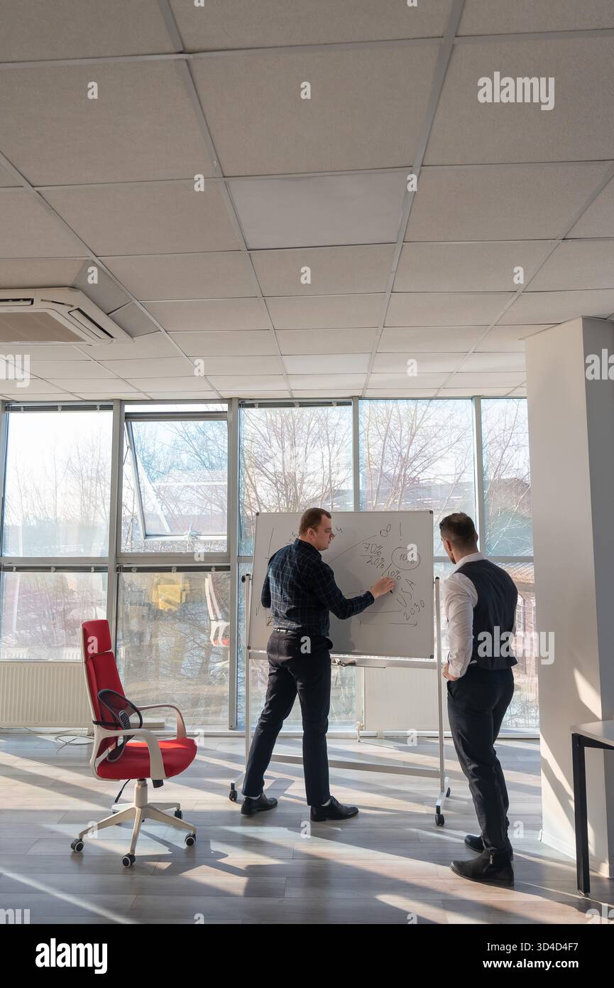 Two Caucasian men discussing work at a white board Stock Photo - Alamy