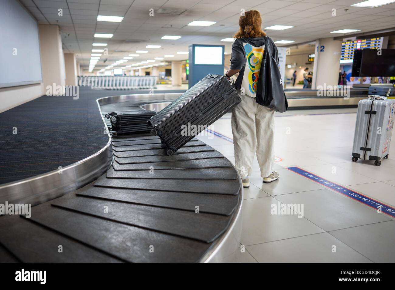 Woman traveler picking up luggage from conveyor line at arrival area ...
