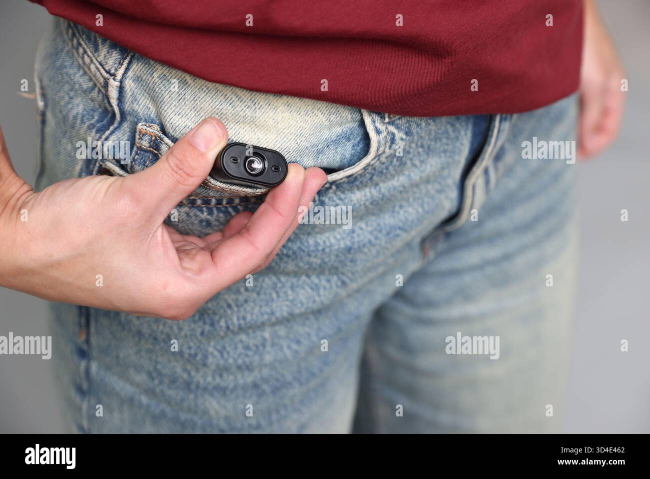 Young woman with hidden spy camera in her pocket on light grey ...