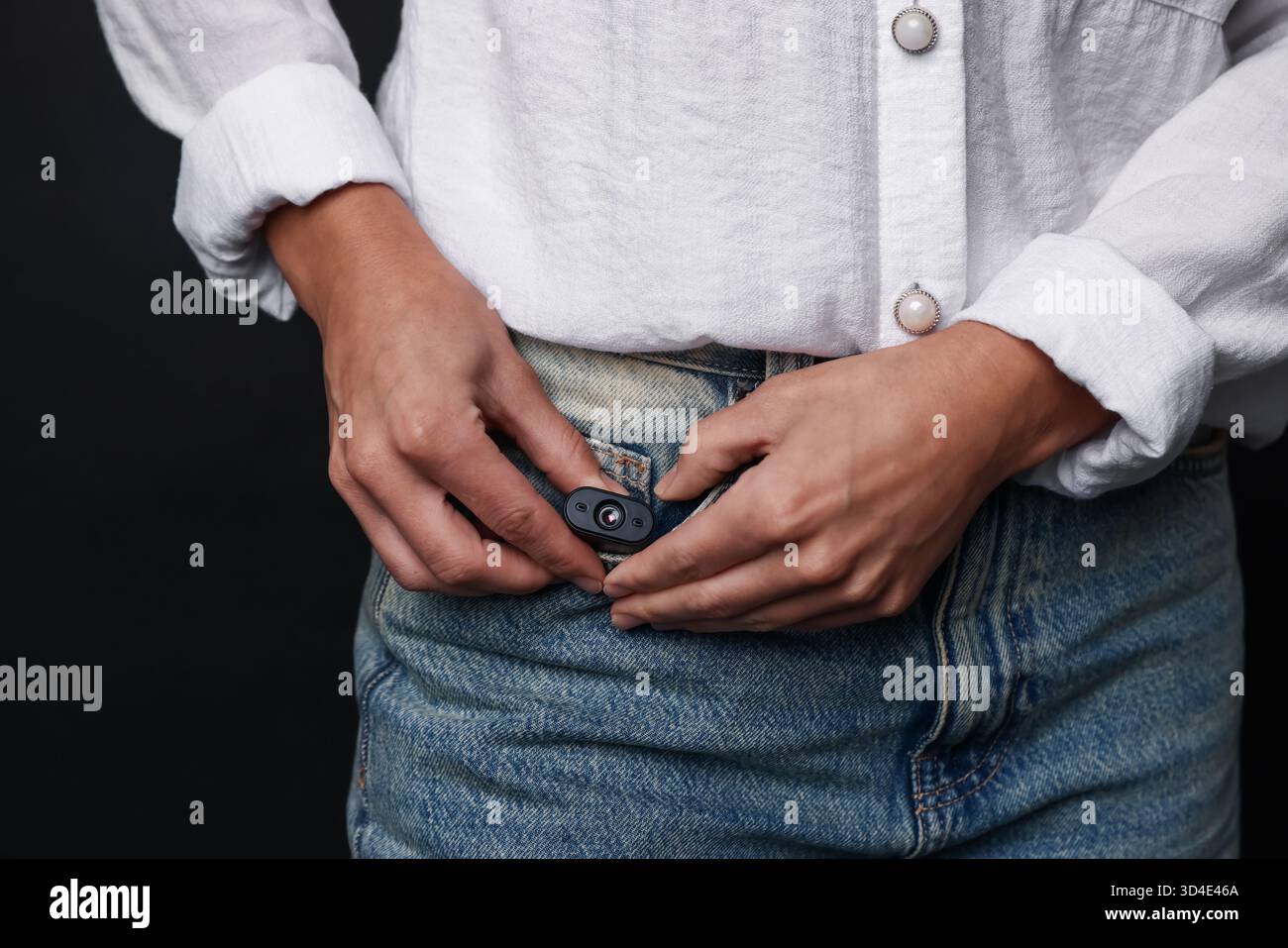 Young woman with hidden spy camera in her pocket on black background ...
