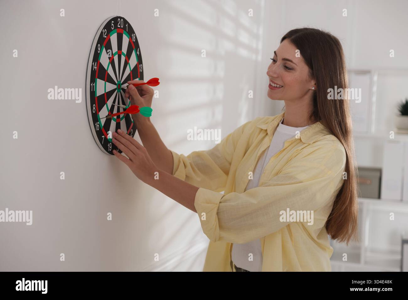 Happy woman with darts near dartboard in office Stock Photo - Alamy