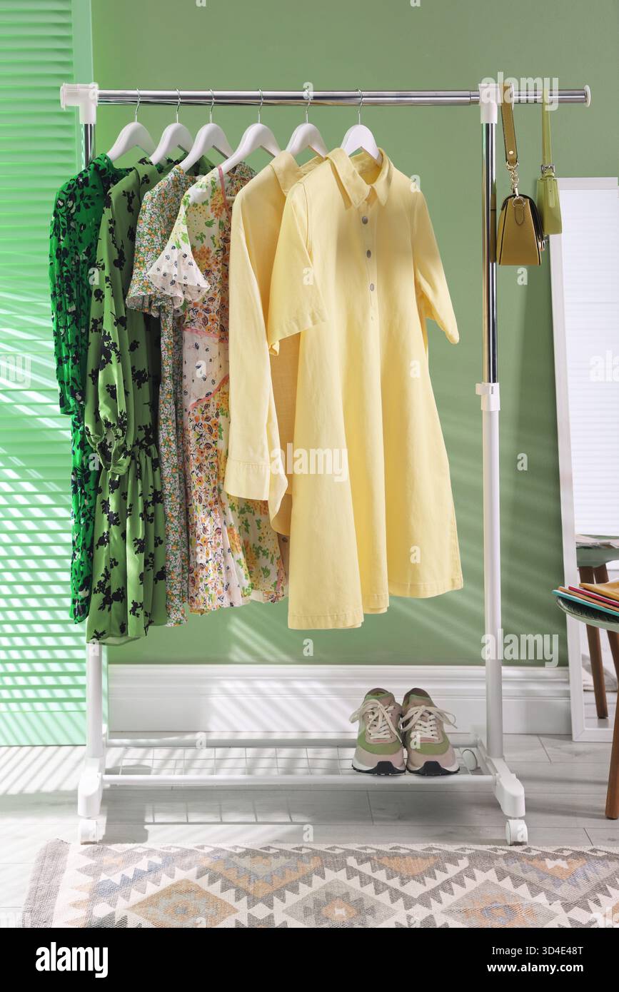 Different women's clothes hanging on rack near green wall indoors Stock ...