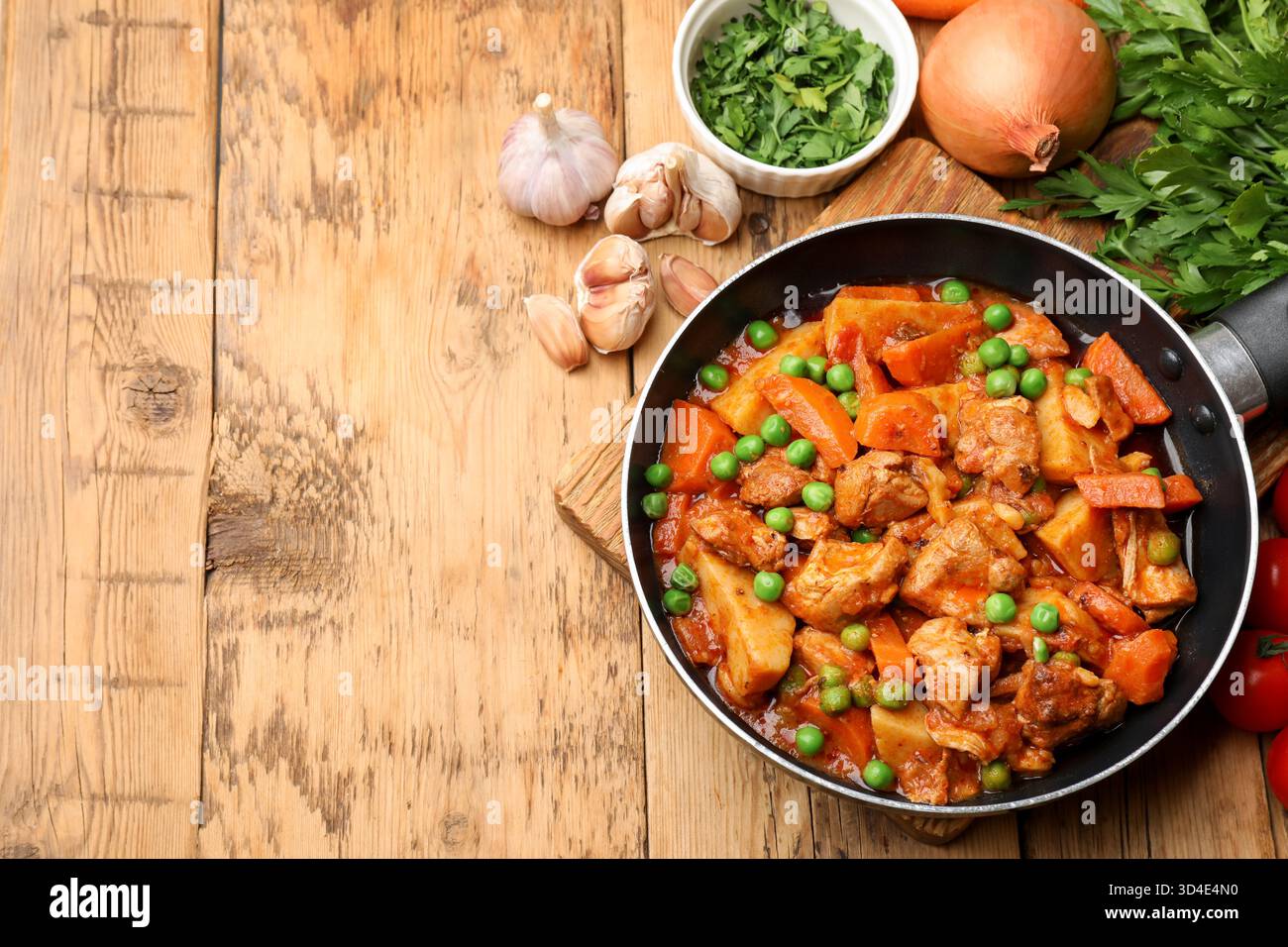 Delicious cooked stew in frying pan and ingredients on wooden table ...