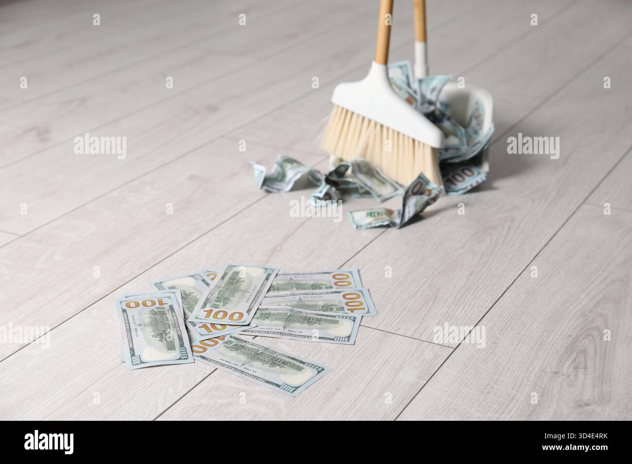 Sweeping dollar banknotes with broom into dustpan on light wooden floor ...
