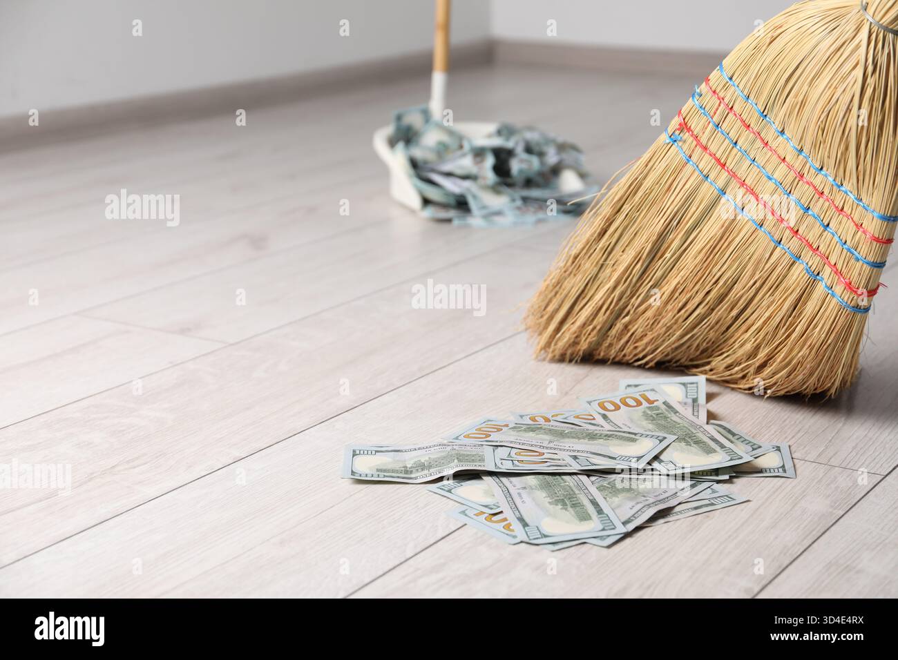 Sweeping dollar banknotes with broom into dustpan on light wooden floor ...